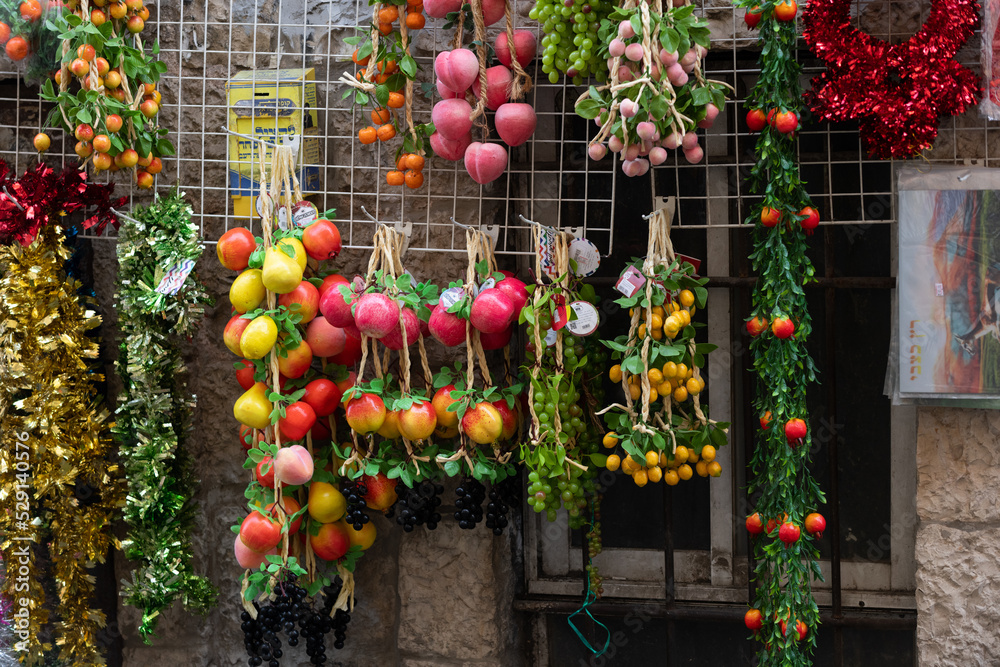 Strings of brightly colored, plastic fruits are sold on a street in ...