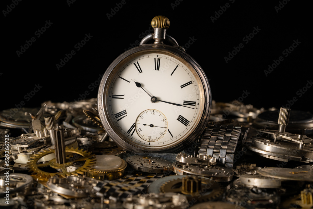 Old silver pocket watch on a pile of gears, gearwheels, cogwheels and ...