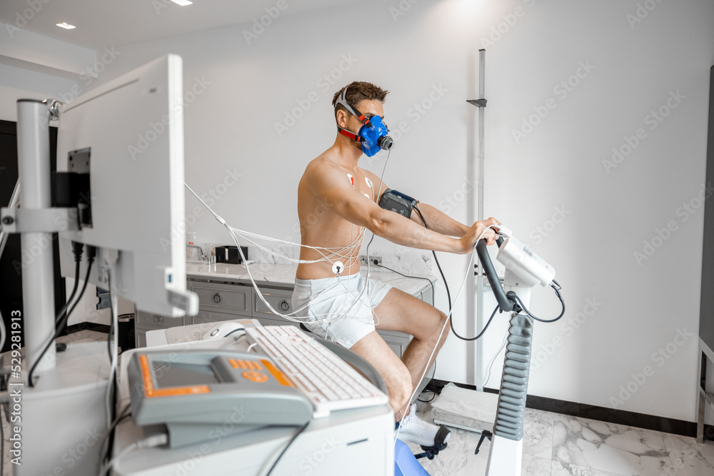 Man athlete with breath mask and electrodes training on bike simulator ...