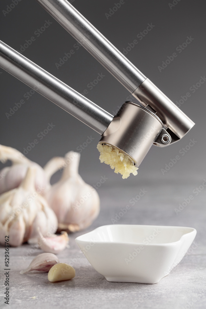 Squeeze the garlic with a garlic press. Stock Photo | Adobe Stock