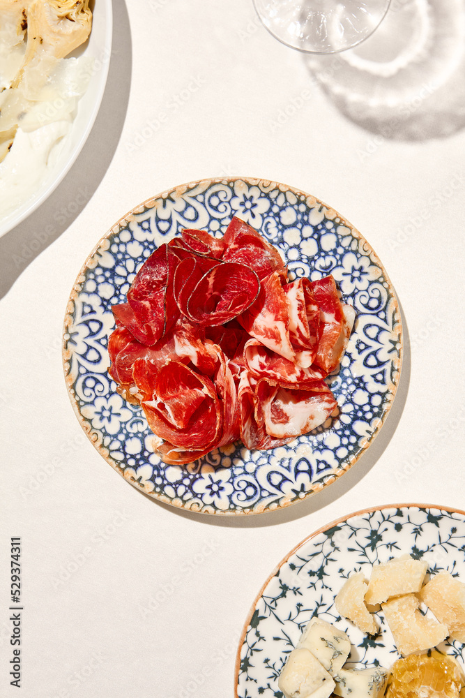 Meat antipasti on ceramic plate on white table with hard shadow. Meat ...