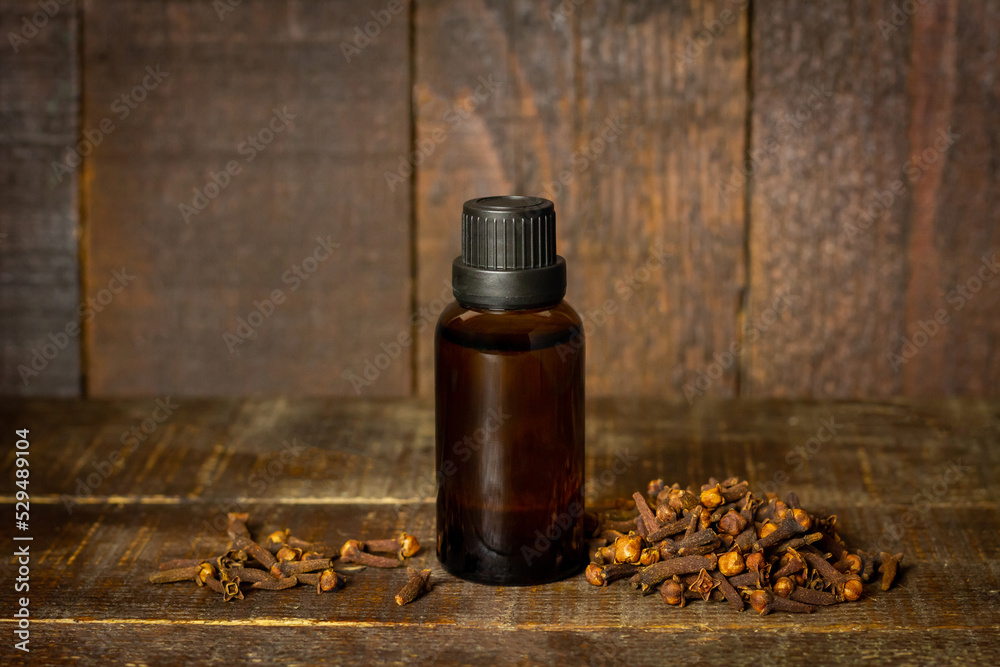 Essential oil of cloves in bottle and dry cloves on rustic wooden ...