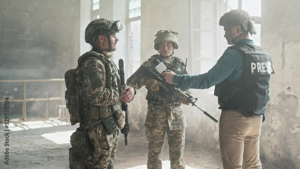 Male war journalist holding microphone taking interview from military ...