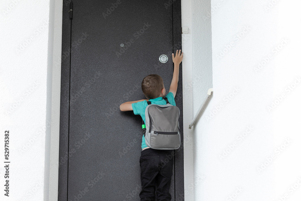 White Caucasian little child, school boy pushes doorbell on closed ...