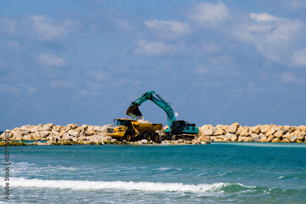 An excavator and a mining truck move stones into the sea. Construction ...
