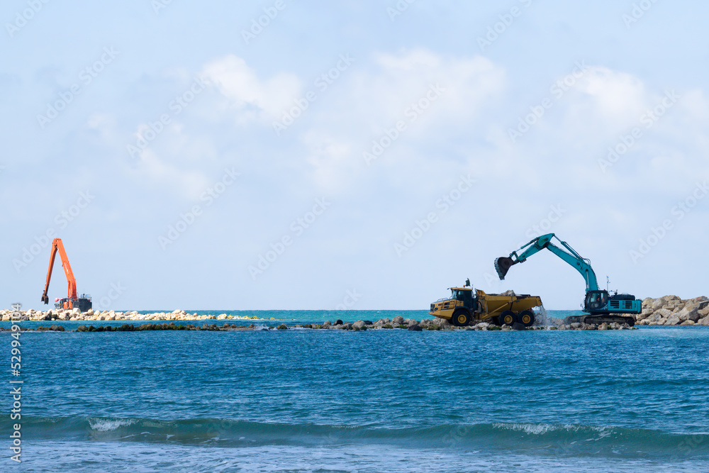 An excavator and a mining truck move stones into the sea. Construction ...