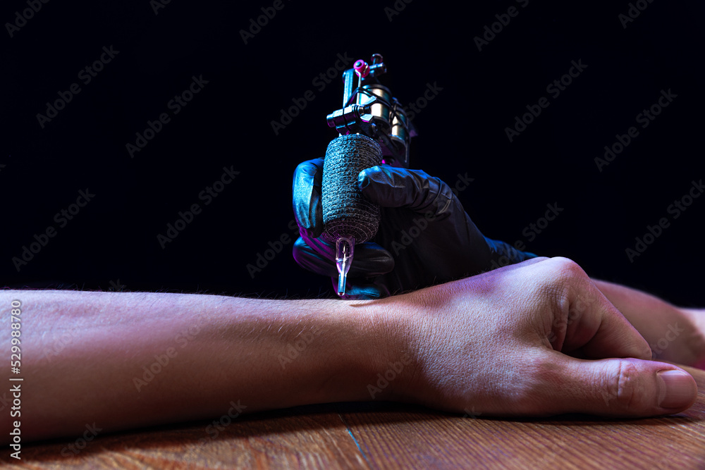 Tattooer master's hand in black glove making tattoo art on male hand ...