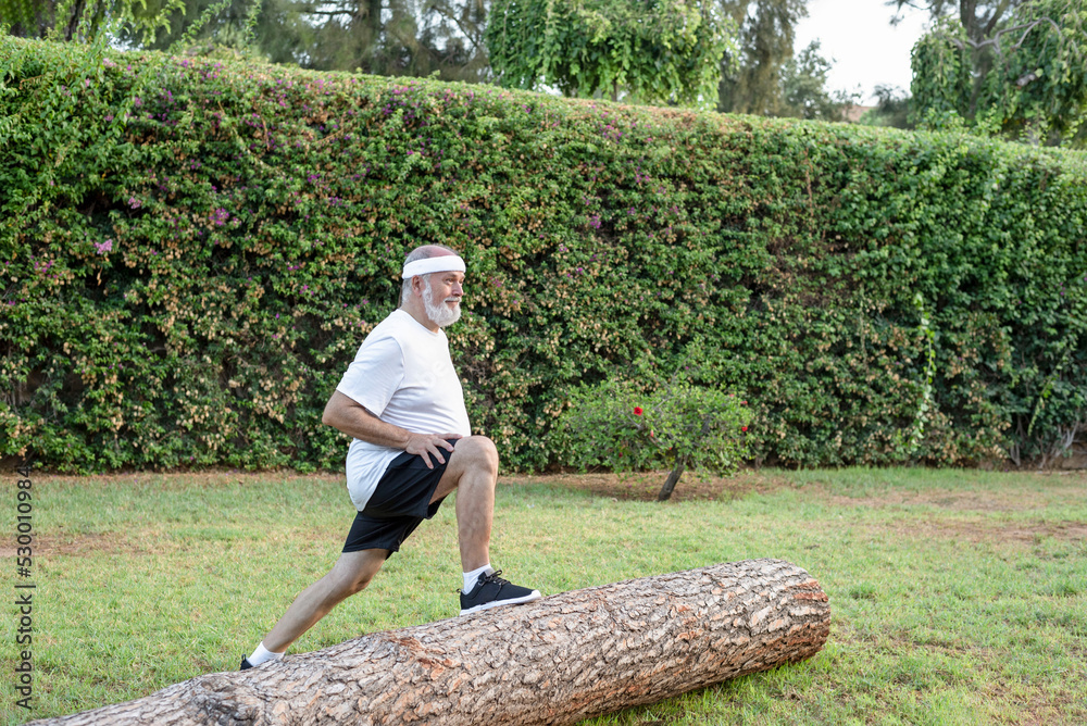 Older man doing front squat on one leg forward in city park during ...