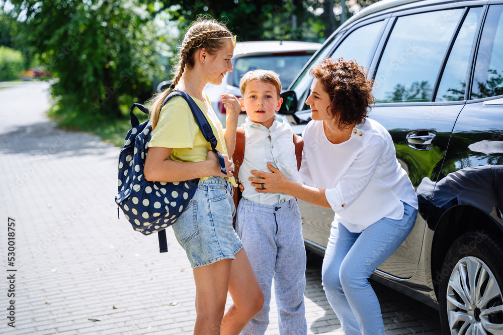 Smiling happy mother bringing daughter and son back to school saying ...
