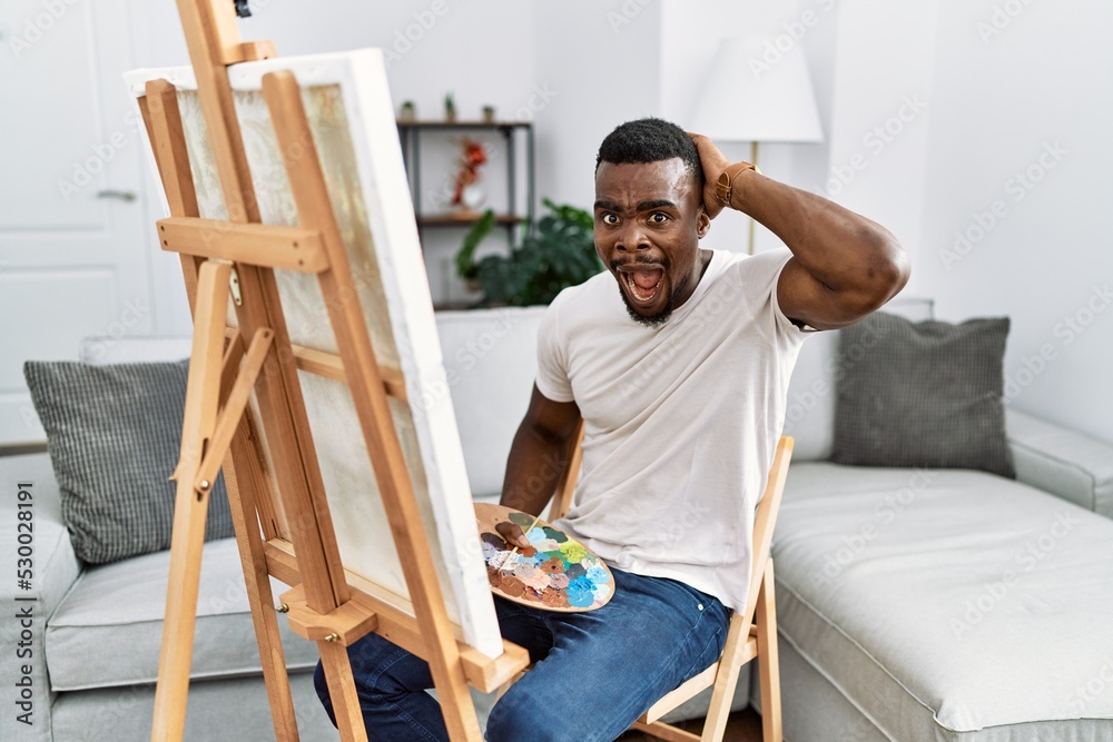 Young african man painting on canvas at home crazy and scared with ...