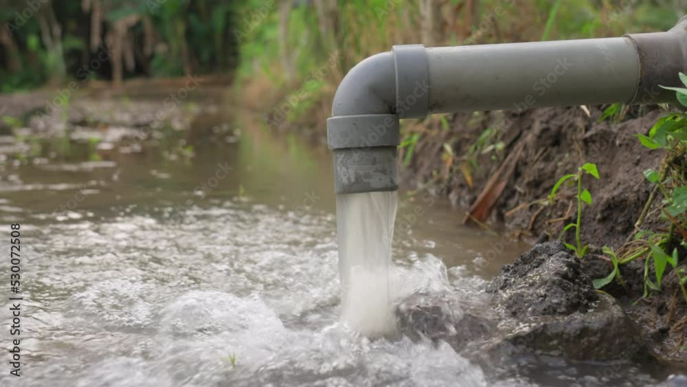 Close-up view of water flow streaming out of plastic pipe onto a ...