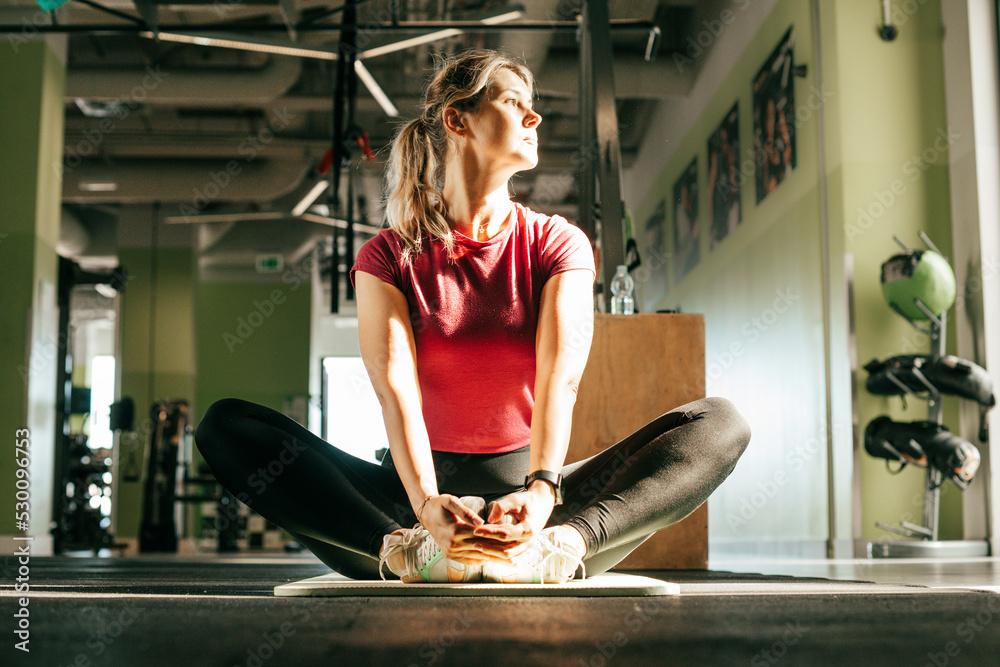 Plus Size Girl Sit On Mat In Fitness Gym Holding Feet By Hands And