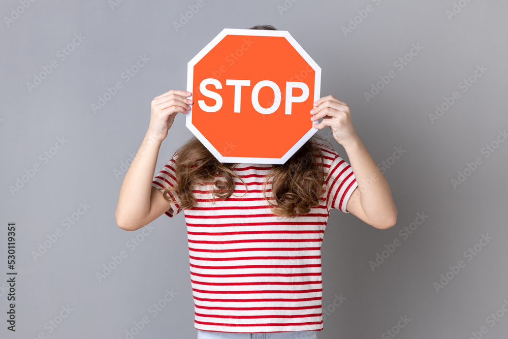 Little girl in striped T-shirt covering face with Stop symbol ...