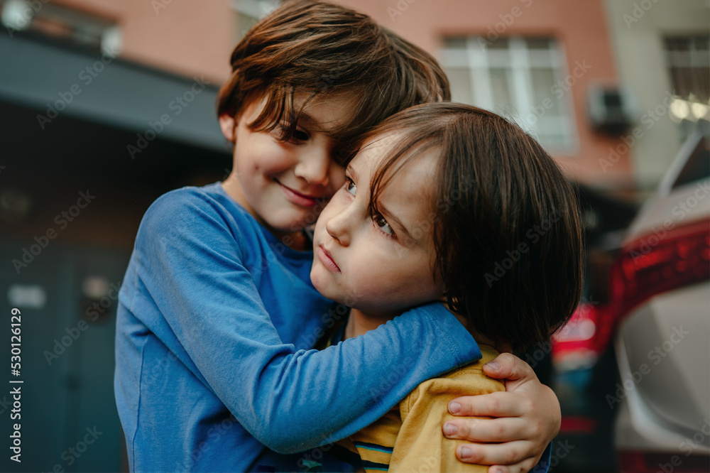 Two boys, two brothers are standing on the street and hugging tightly ...