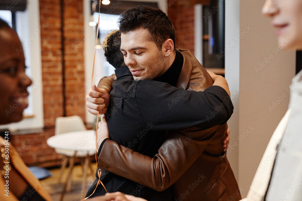 Happy young man in leather jacket giving hug to black woman in denim ...