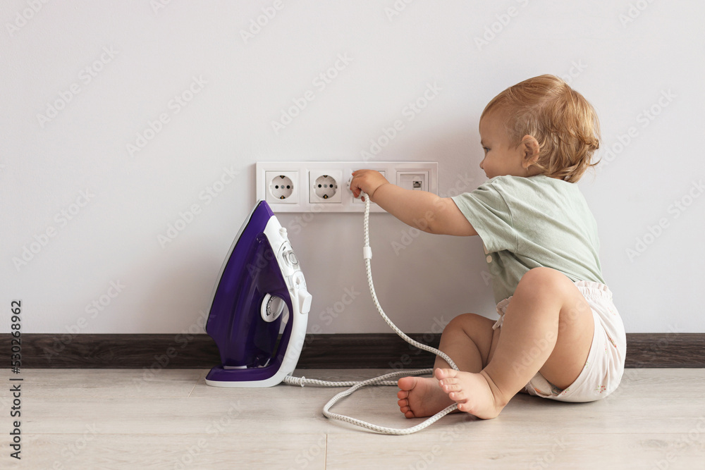 Cute baby playing with electrical socket and iron plug at home ...