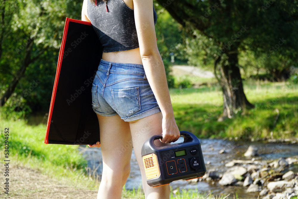 Woman out in nature carries solar panel and power station for ...
