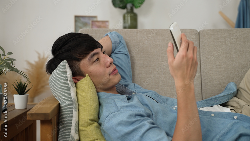 Foto de side view of happy asian guy lying on the sofa celebrating for ...