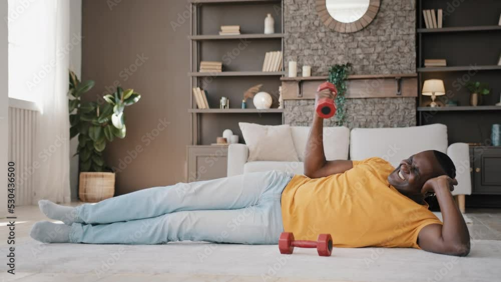 Active senior sportsman afro powerful man pumping biceps at home lying ...