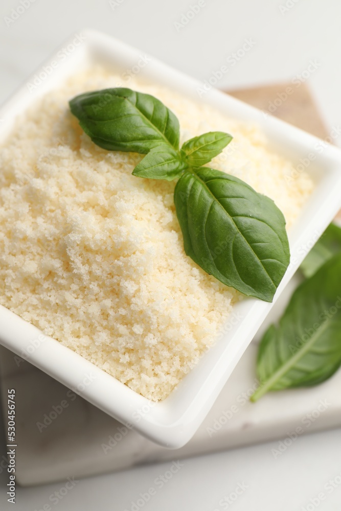 Square bowl with grated parmesan cheese and basil on white table, above ...