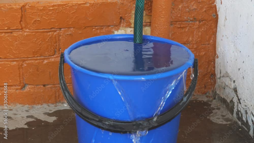The water from the hose has filled the bucket and is overflowing Stock ...
