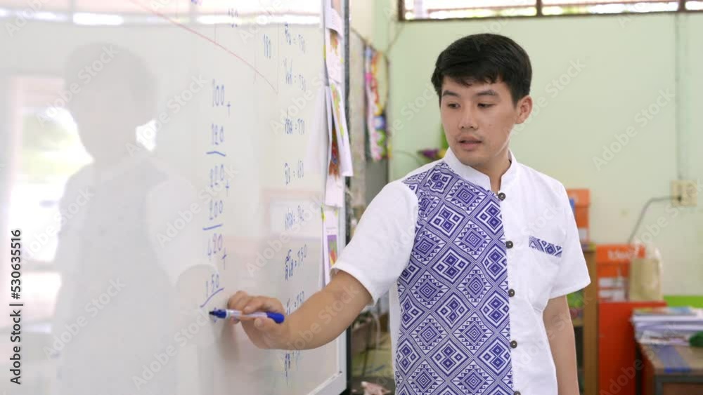An Asian male teacher teaches math and writes the numbers on the board ...