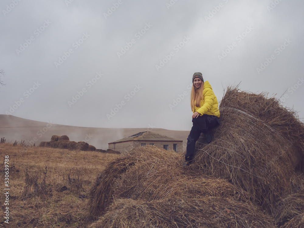 Laughing woman sits on rolled haystacks in an abandoned area among the ...