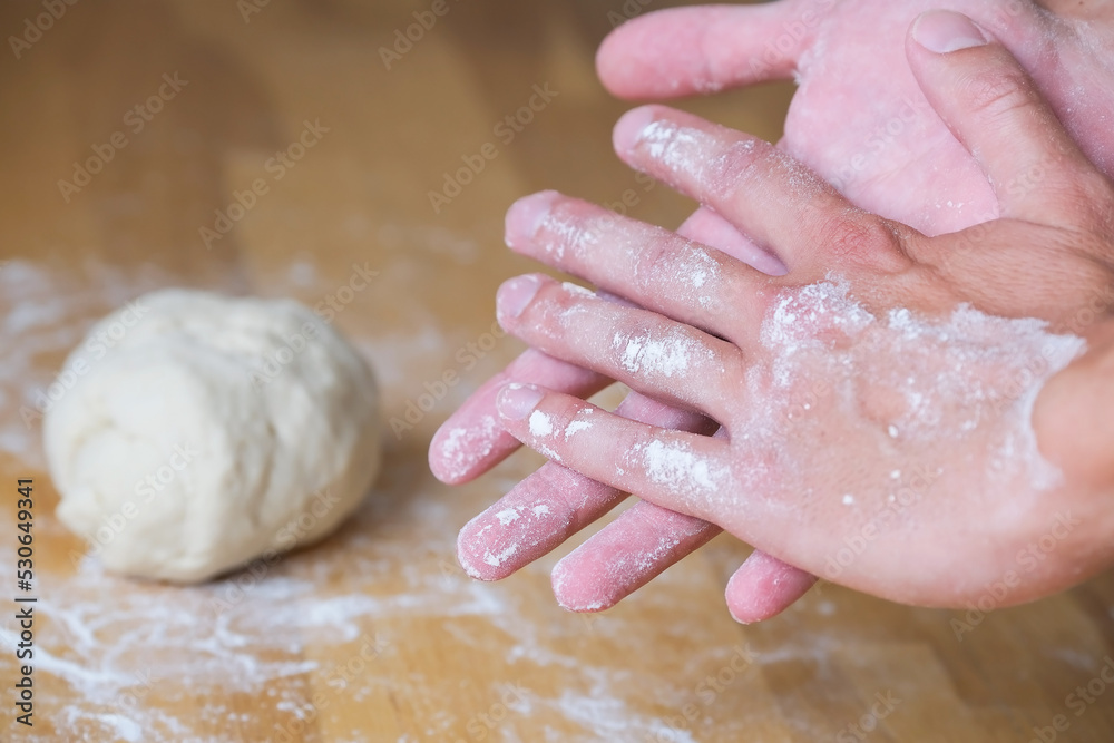 Сook shakes off flour from his hands against the background of a lump ...
