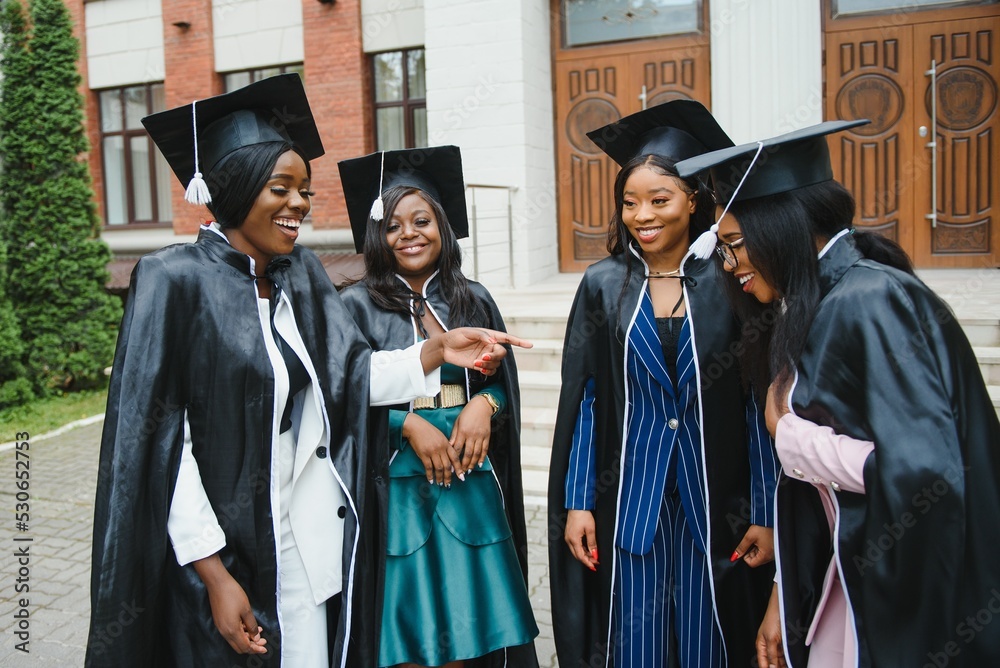 young graduates standing in front of university building on graduation ...