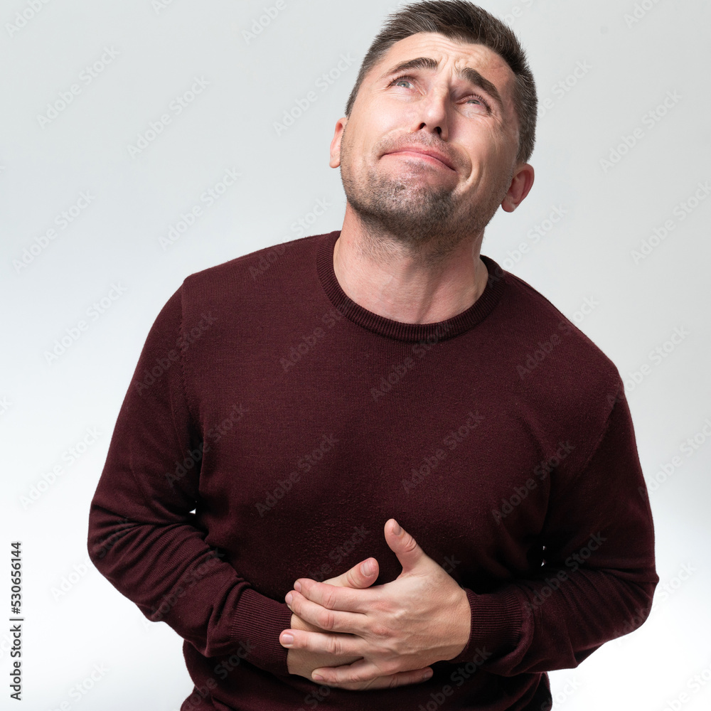 A man touches his stomach with two hands, on a white background with ...