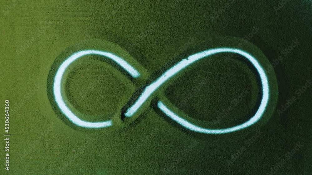 Hand drawing the Infinity symbol in the Green Sand. Male hand writes ...