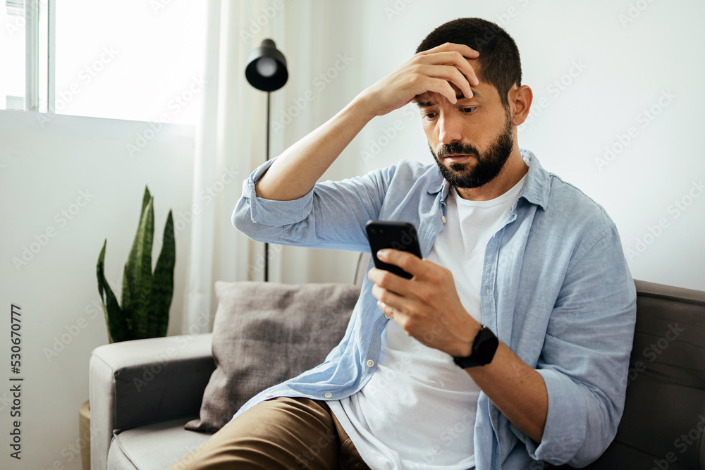Sad man checking smartphone sitting on a sofa at home Stock Photo ...
