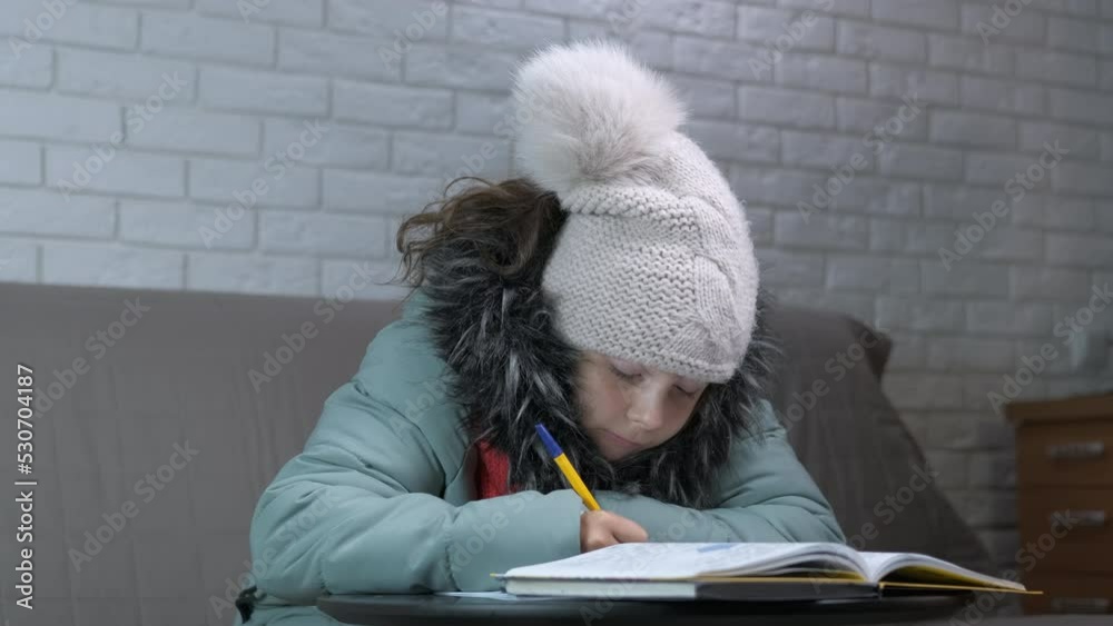 Do homework in cold room. A child in winter clothes try to study in ...