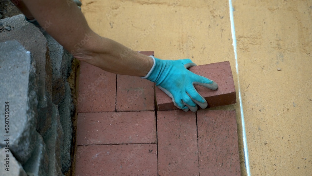 Overhead closeup of womans hand putting brick pavers onto a sand base ...