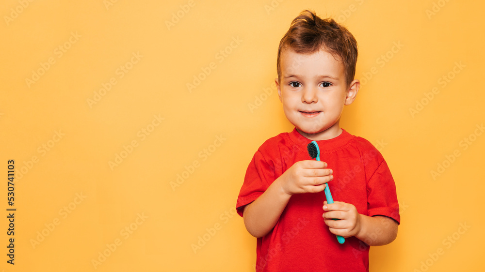 The happy kid is holding a toothbrush on a yellow background and ...