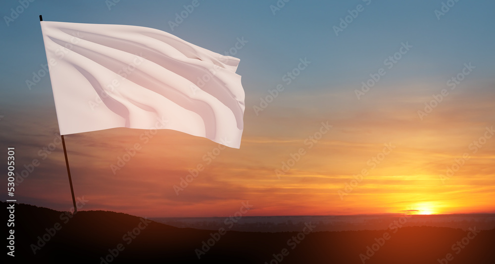 White flag waving in the wind on flagpole against the sunset sky with ...