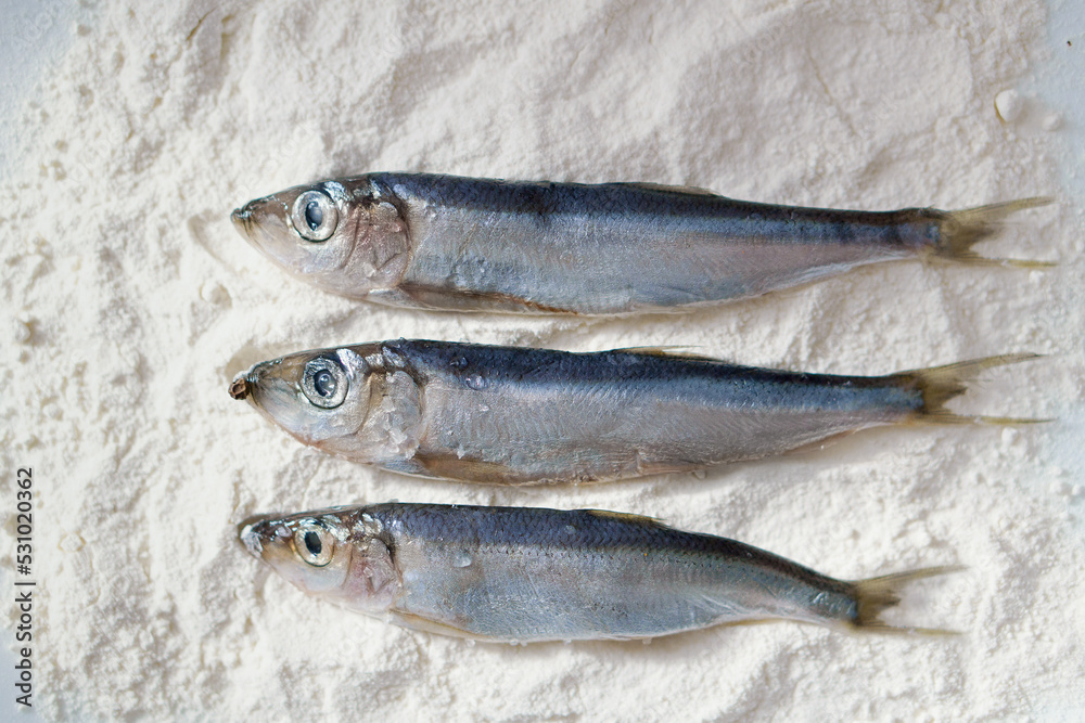 Three herrings on a plate with flour. Stages of cooking fish ...