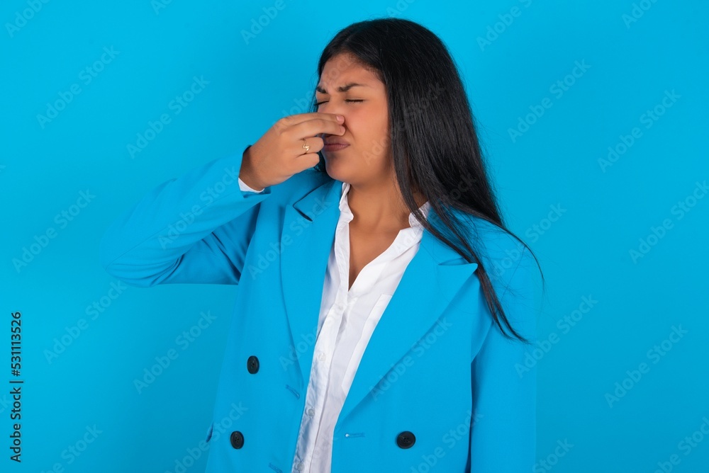 Young latin woman wearing blue blazer blue background smelling ...