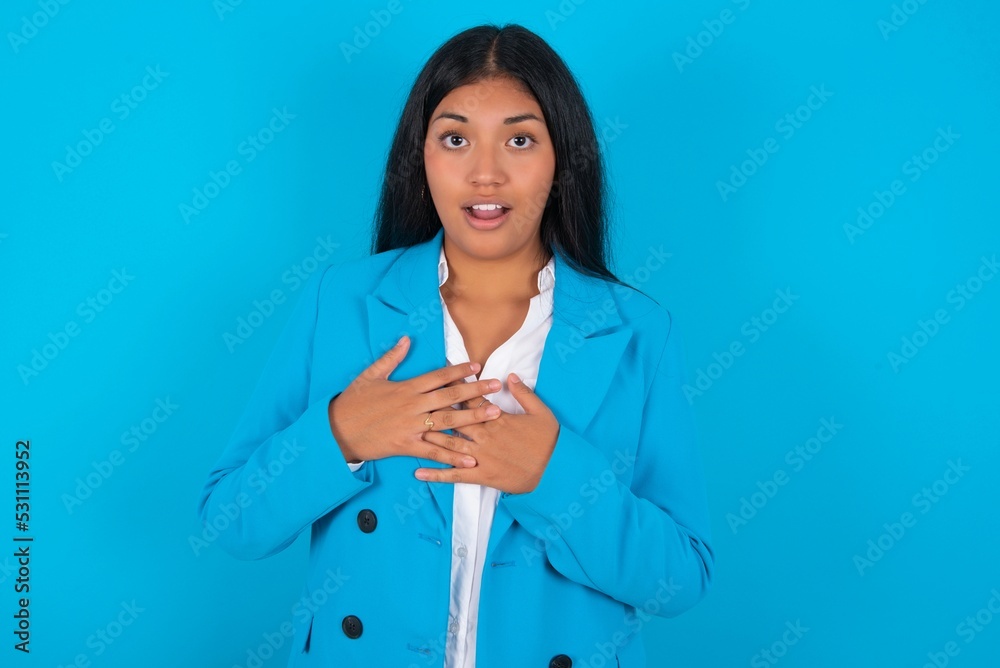 Scared Young latin woman wearing blue blazer blue background looks with ...