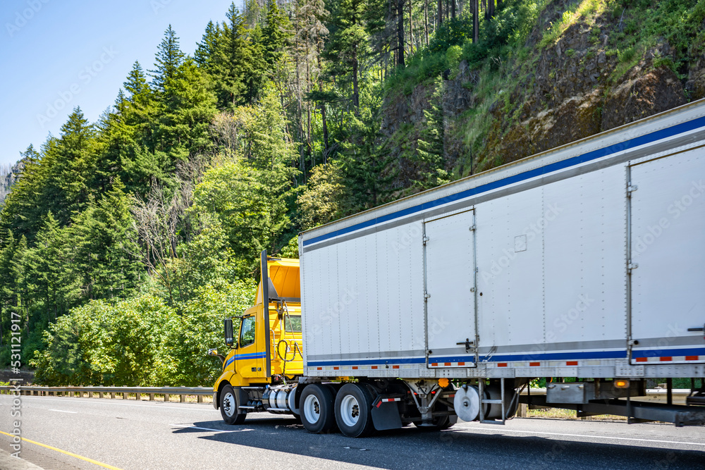 Day cab yellow big rig semi truck with roof spoiler driving with dry ...