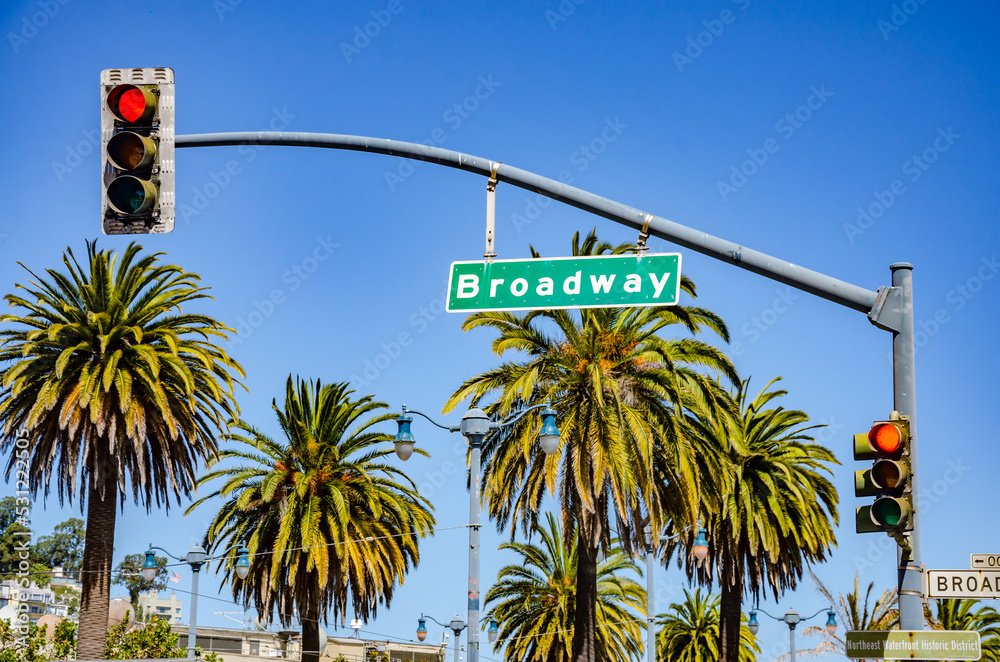 A street sign for Broadway hanging from the crossbar of a traffic light ...