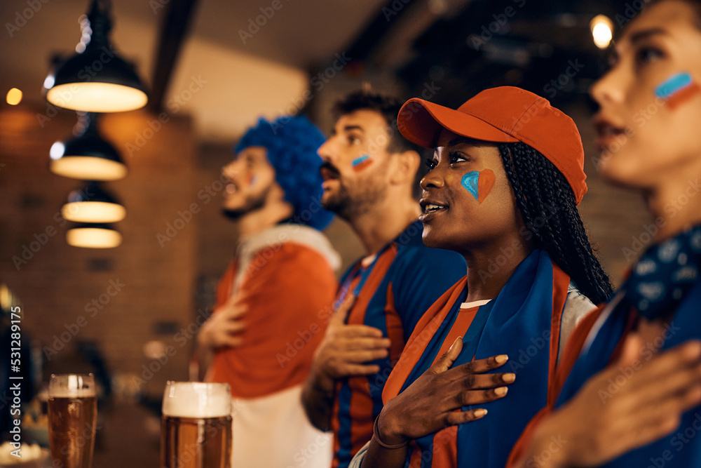 Group of fans with hand on heart singing national anthem while watching ...