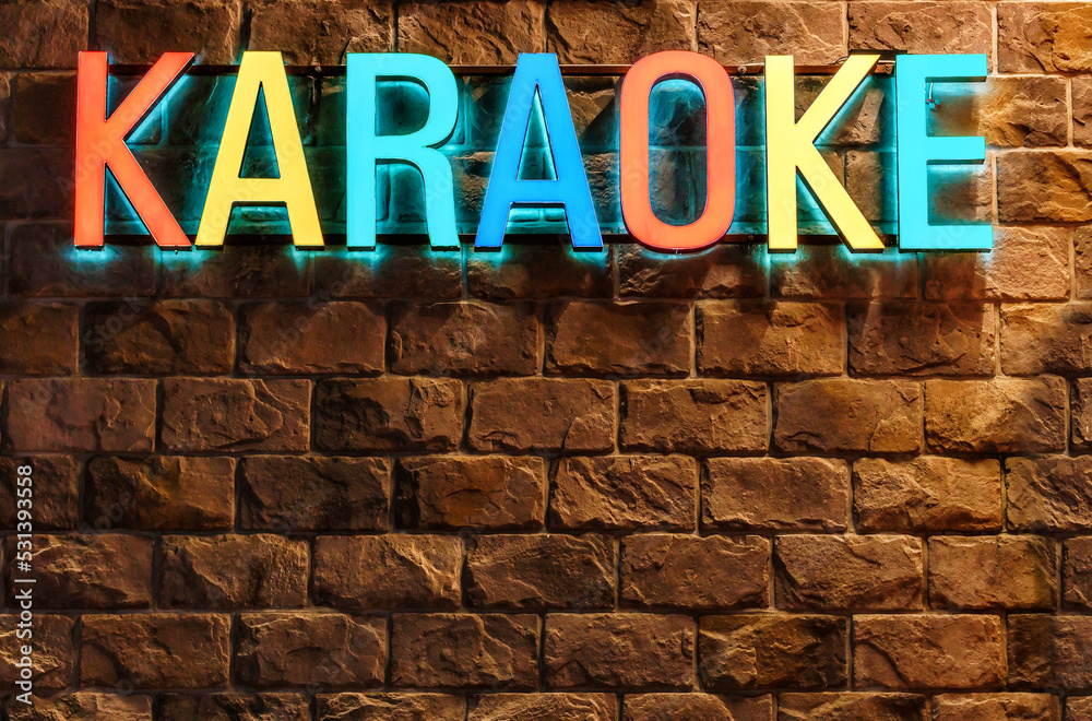 Colorful neon illuminated Karaoke sign on stone building wall ...