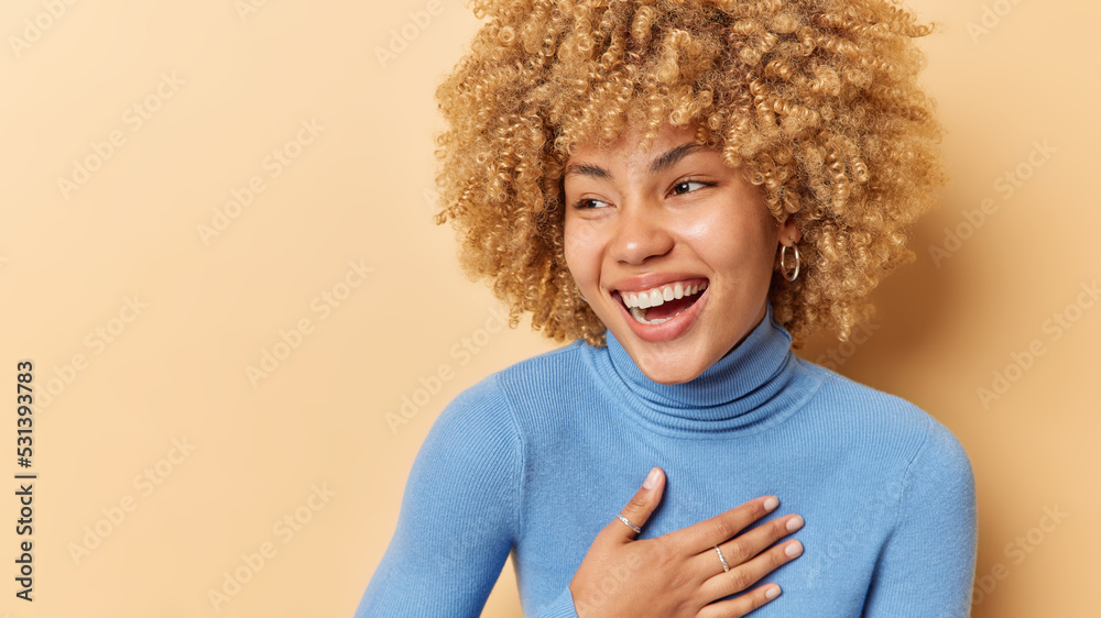 Portait of happy overjoyed woman keeps hand on chest laughs joyfully ...