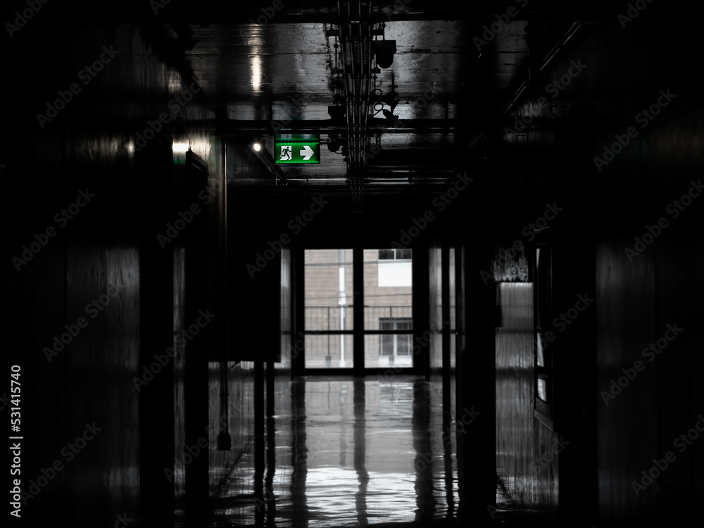 Green exit fire sign hanging on ceiling on dark mysterious corridor in ...