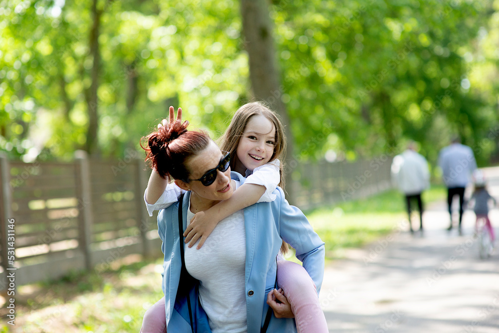 Cute young daughter on a piggy back ride with her mother.Happy family ...