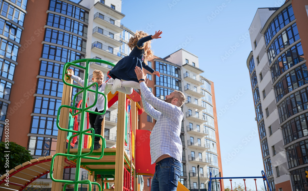 Happy dad catching cheerful daughter, jumping from slide at playground ...