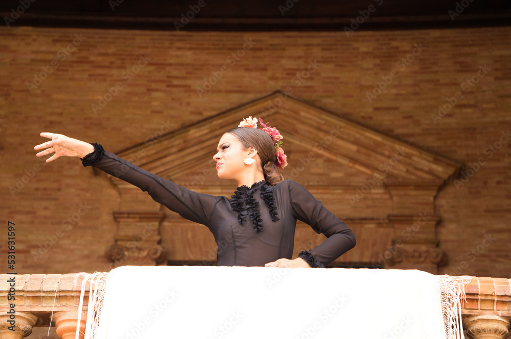 A beautiful teenage flamenco dancer with brown hair stands on a balcony ...