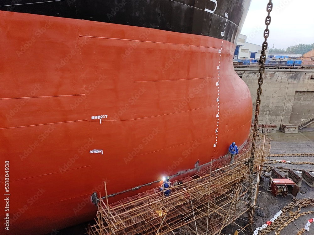 A red ship hull with draft mark and a man or worker who's sitting on ...