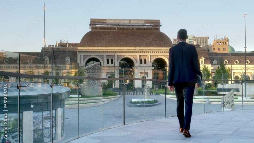man in strict blue suit with laptop in his hands walks through park ...